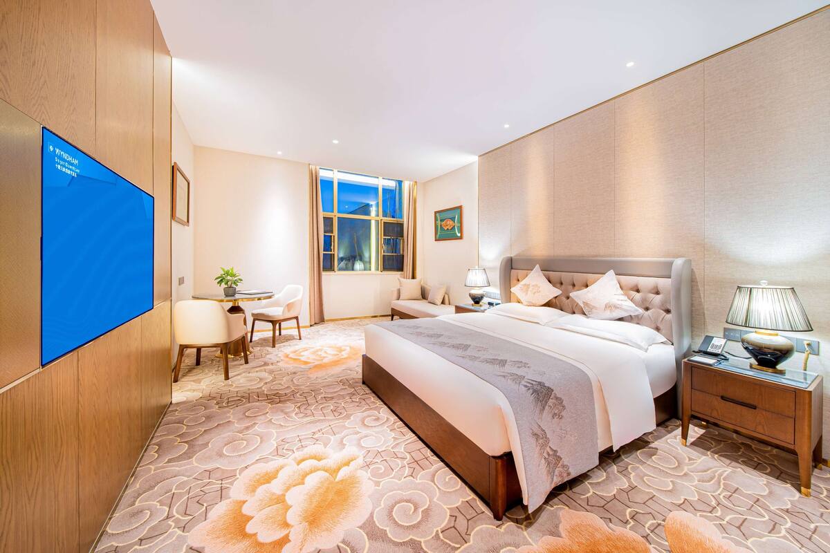 Quarto de hotel moderno com uma cama grande, uma escrivaninha e uma televisão na parede.