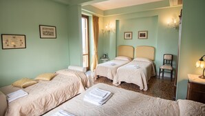 Quarto de hotel com duas camas, uma cadeira, uma mesinha e um espelho.