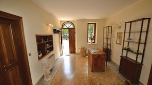 Um corredor com piso de azulejos, armários de madeira, um pedestal branco e uma porta.