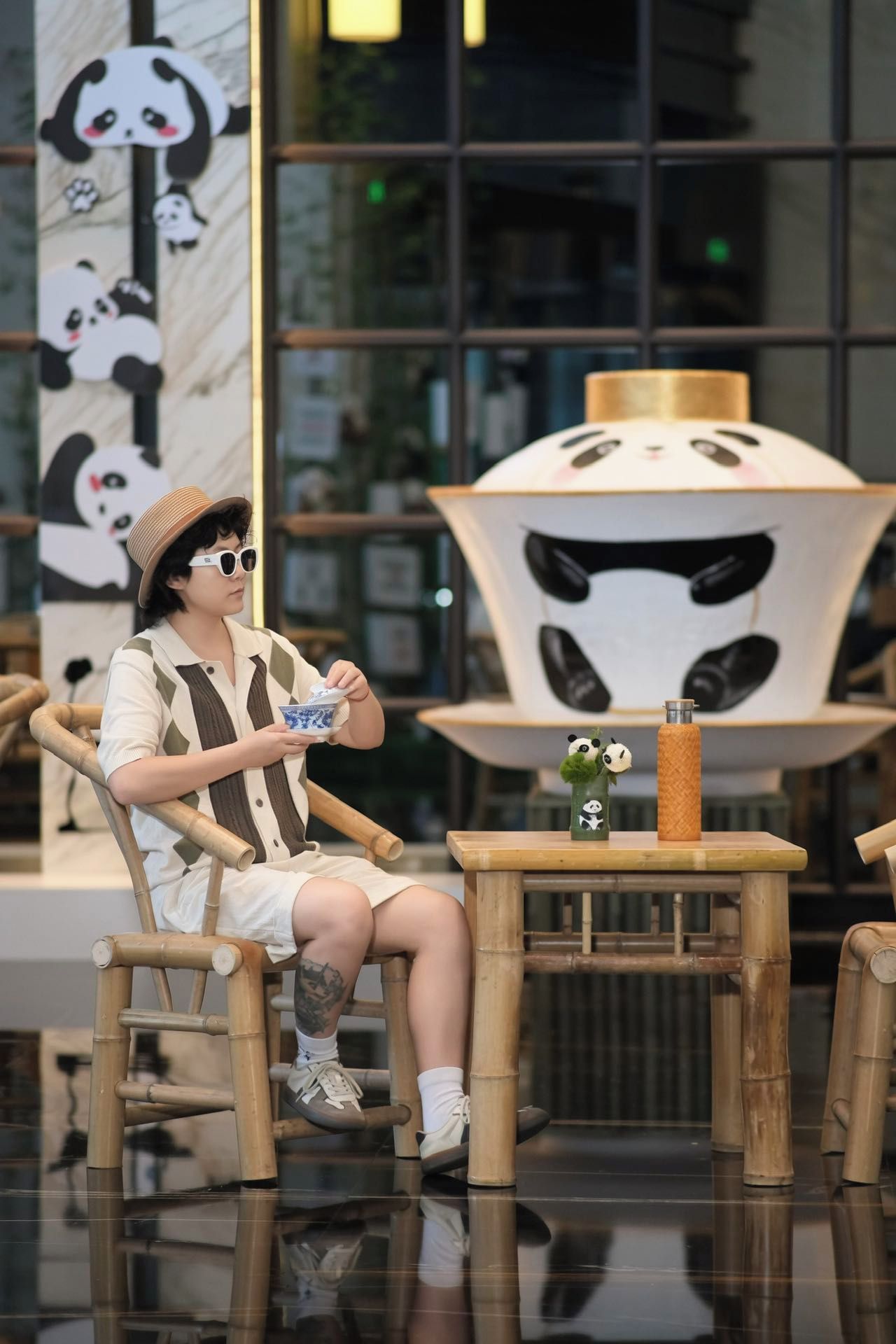 Uma pessoa sentada à mesa com uma luminária temática de panda e objetos decorativos.