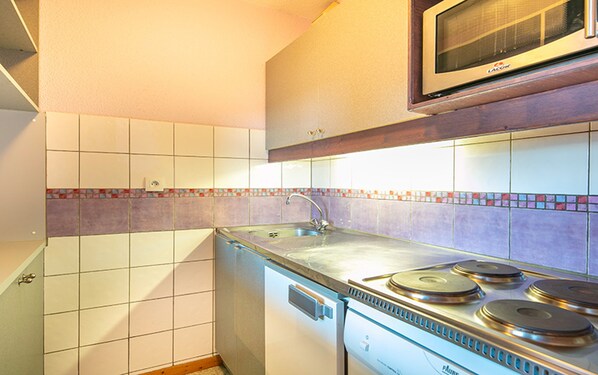 Uma cozinha com armários brancos, painel de azulejos, pia de aço inoxidável e fogão embutido.