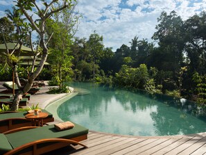 Uma área de piscina tranquila com espreguiçadeiras e um deck de madeira, cercada por vegetação exuberante e árvores.