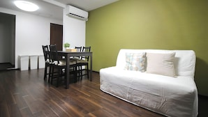 Um quarto com uma mesa de jantar, cadeiras, um sofá branco e uma parede verde decorativa.