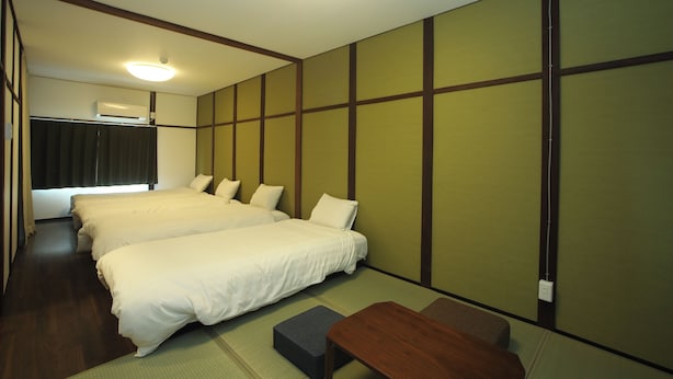 Quarto de hotel com duas camas, um banco de madeira, uma mesinha e uma luminária no teto.