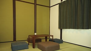 Um espaço com tatames, uma mesa de madeira baixa, dois almofadas e uma janela com cortina escura.