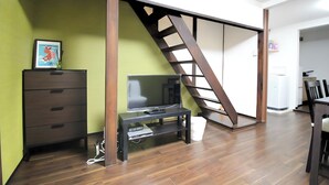 Uma sala de estar com escada de madeira, uma TV em um suporte preto, um aparador e um quadro na parede.