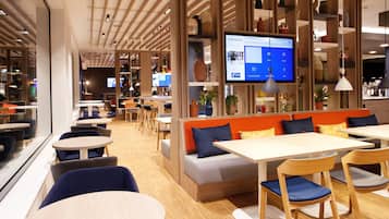 Interior de restaurante moderno com mesas redondas, cabines e uma grande tela de televisão exibindo um menu.