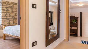 Quarto com cama, parede de pedra, um espelho grande e banheiro visível por uma porta aberta.