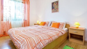 Um quarto com cama, duas mesinhas de cabeceira, um criado-mudo, um tapete verde e um quadro na parede.