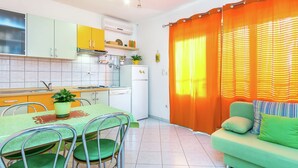 Cozinha compacta com área de refeições, sofá e cortinas laranja.