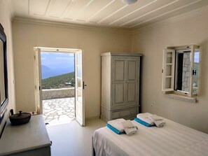 Quarto com cama, guarda-roupa, mesinha e porta que dá para uma varanda com vista para o mar.