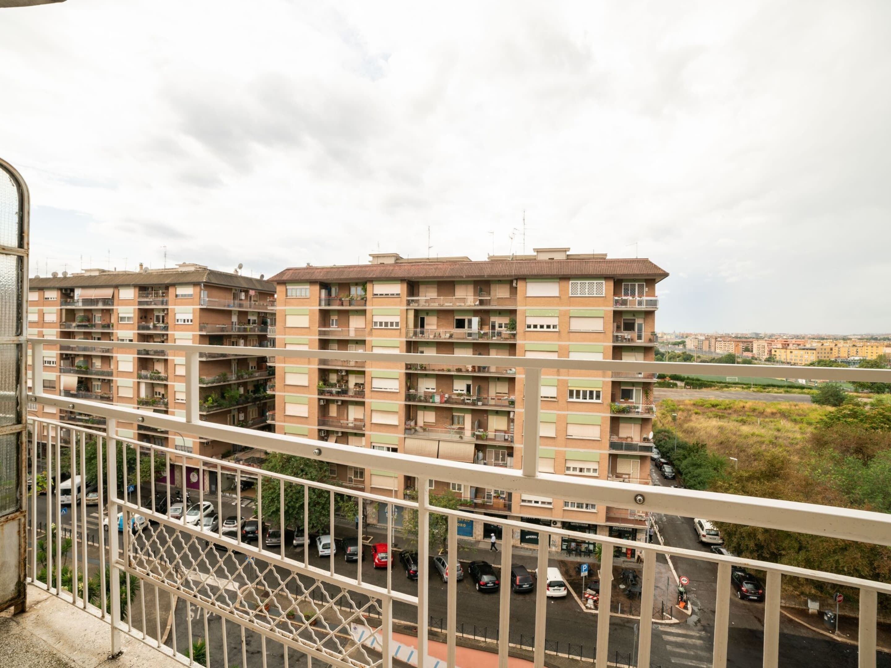 Um edifício residencial com várias andares, varandas, área de estacionamento na frente e vista do bairro ao redor.