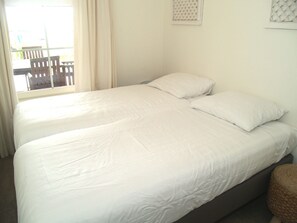 Cama de casal com lençóis brancos em quarto com vista para móveis de exterior.