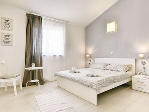Quarto com cama, mesas de cabeceira, uma cadeira e janela com cortinas.