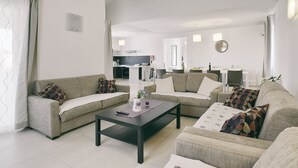 Uma sala de estar moderna com dois sofás, uma mesa de centro e uma cozinha ao fundo.