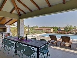 Um alpendre coberto com piscina, área de estar externa e churrasqueira.