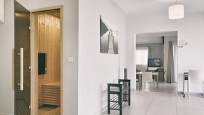 Um interior moderno com uma sauna de madeira, uma área de refeições com cadeiras, uma cozinha com TV e um chão com azulejos brancos.