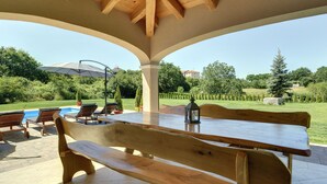 Um pátio externo com um banco de madeira, uma mesa e uma piscina ao fundo.