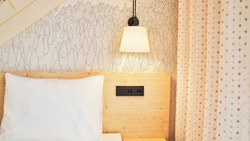 Quarto de hotel com cabeceira de madeira, travesseiro branco, luminária e cortina estampada.