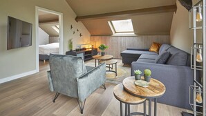 Quarto estilo loft moderno com claraboia, sofá cinza, mesa redonda pequena e cabeça de veado decorativa na parede.