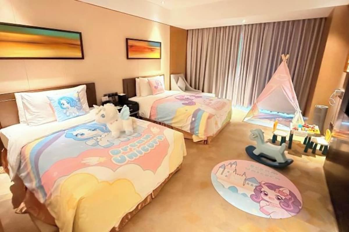 Quarto de hotel com duas camas, uma tenda e uma área de recreação com brinquedos.