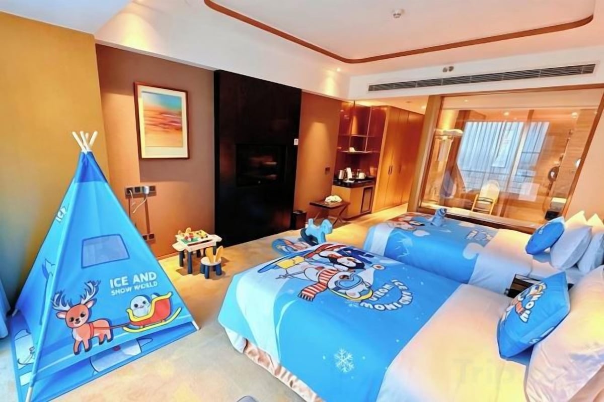 Quarto de hotel com cama grande, mesa pequena, cadeira, uma tenda azul e janela com cortinas.