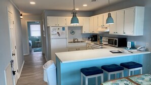 Cozinha moderna com armários brancos, uma ilha central com banquetas, geladeira e micro-ondas.