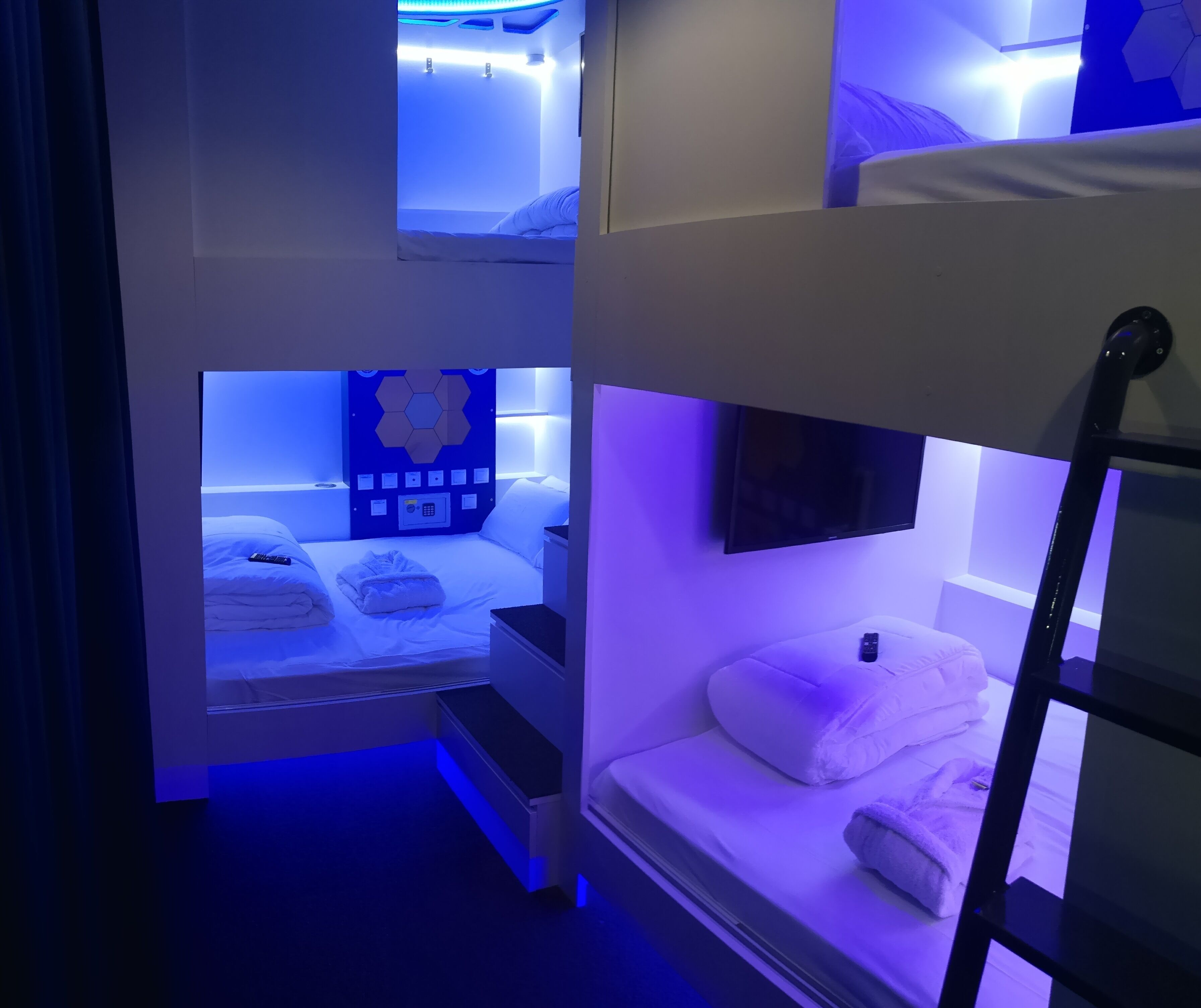 Quarto com beliche, teto iluminado em azul, televisão de tela plana e mesa de cabeceira com controle remoto.