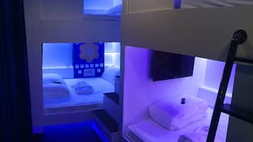 Quarto com beliche, teto iluminado em azul, televisão de tela plana e mesa de cabeceira com controle remoto.