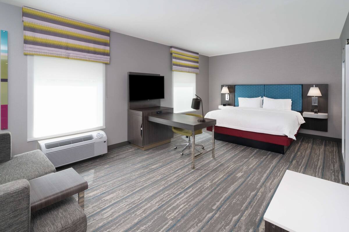 Quarto de hotel com cama, escrivaninha, televisão e ar condicionado.