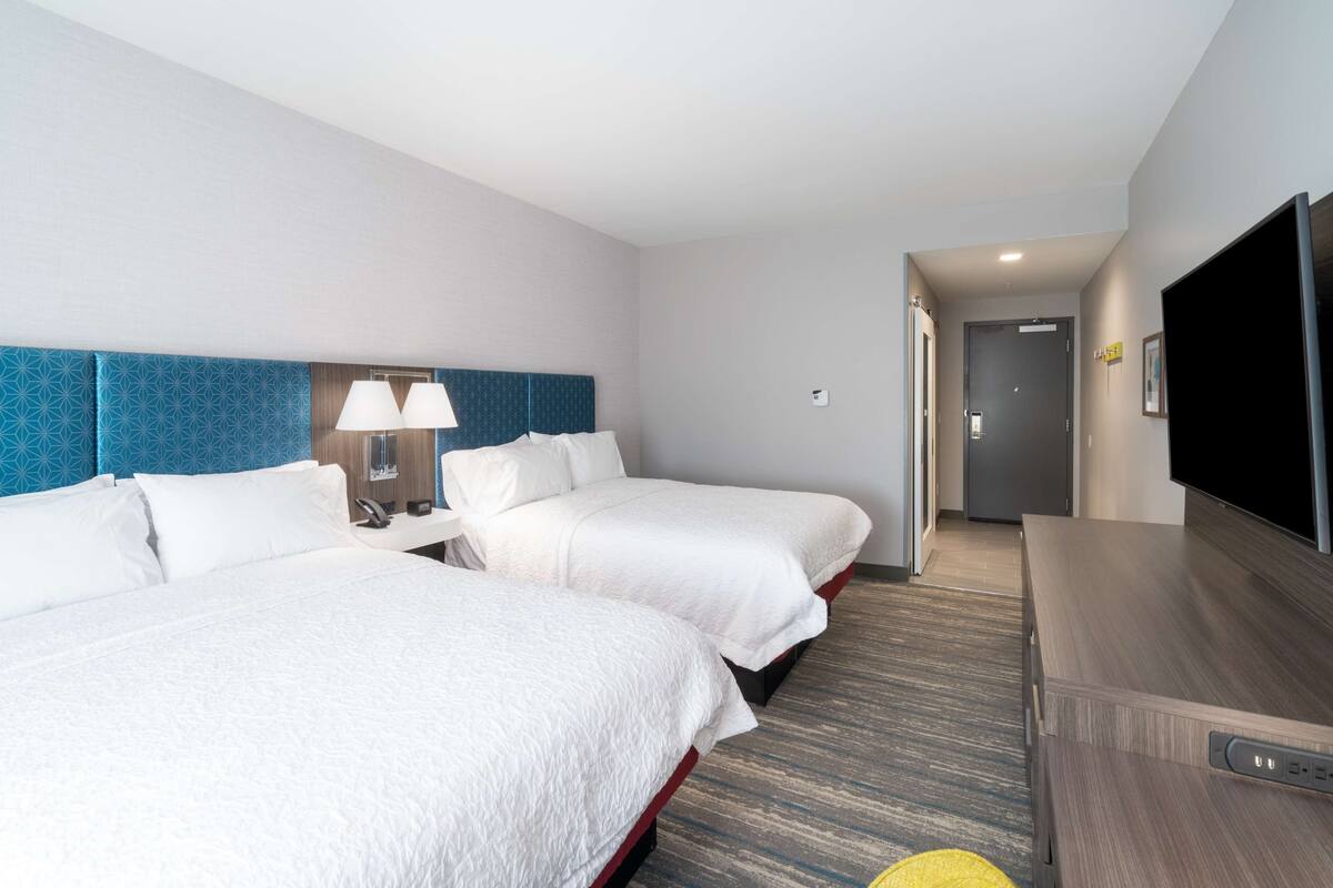 Quarto de hotel com duas camas, uma televisão e uma escrivaninha.