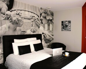 Quarto com cama, laptop, xícara e um mural na parede.
