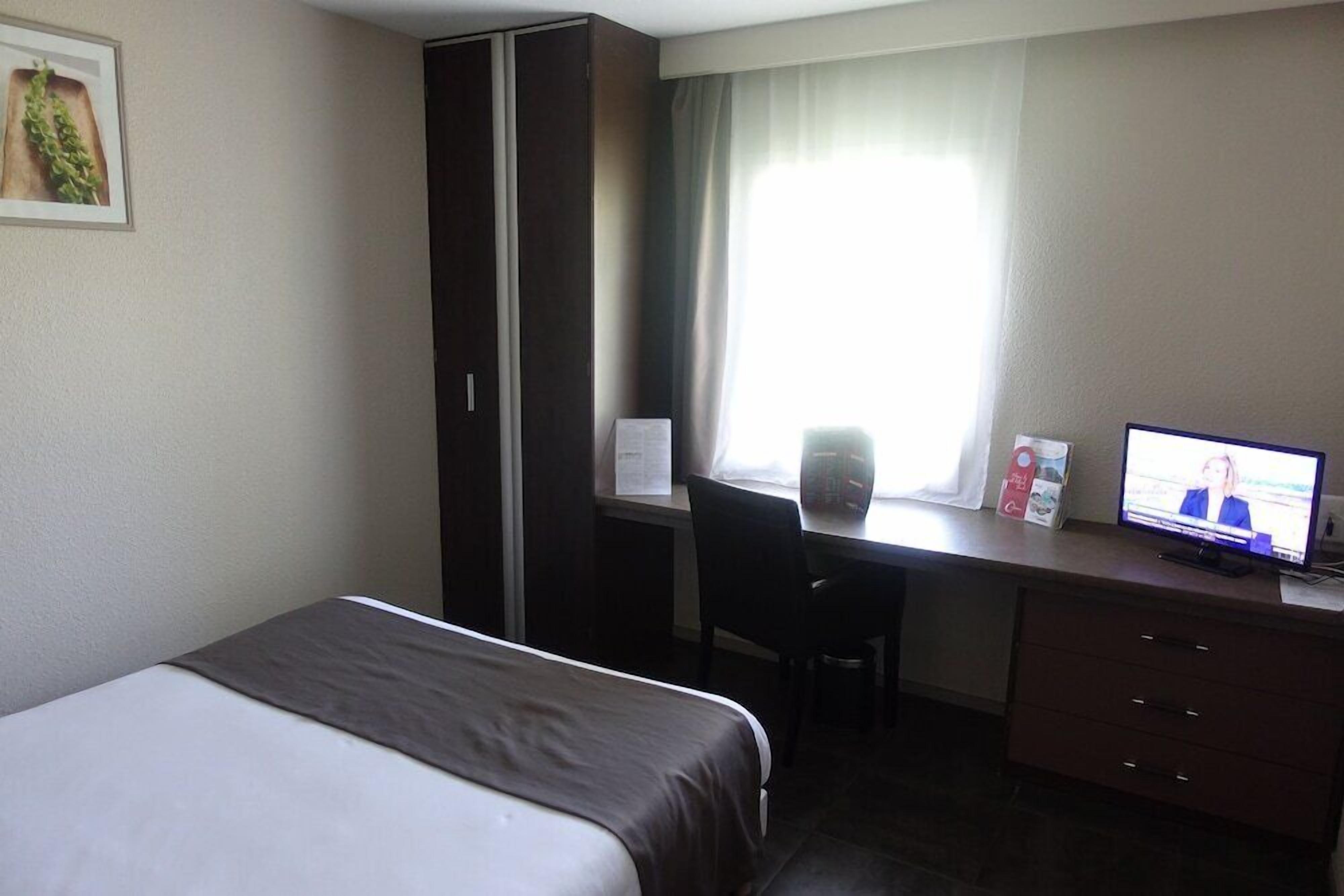 Quarto de hotel com uma cama, uma escrivaninha com computador, uma cadeira e um guarda-roupa.