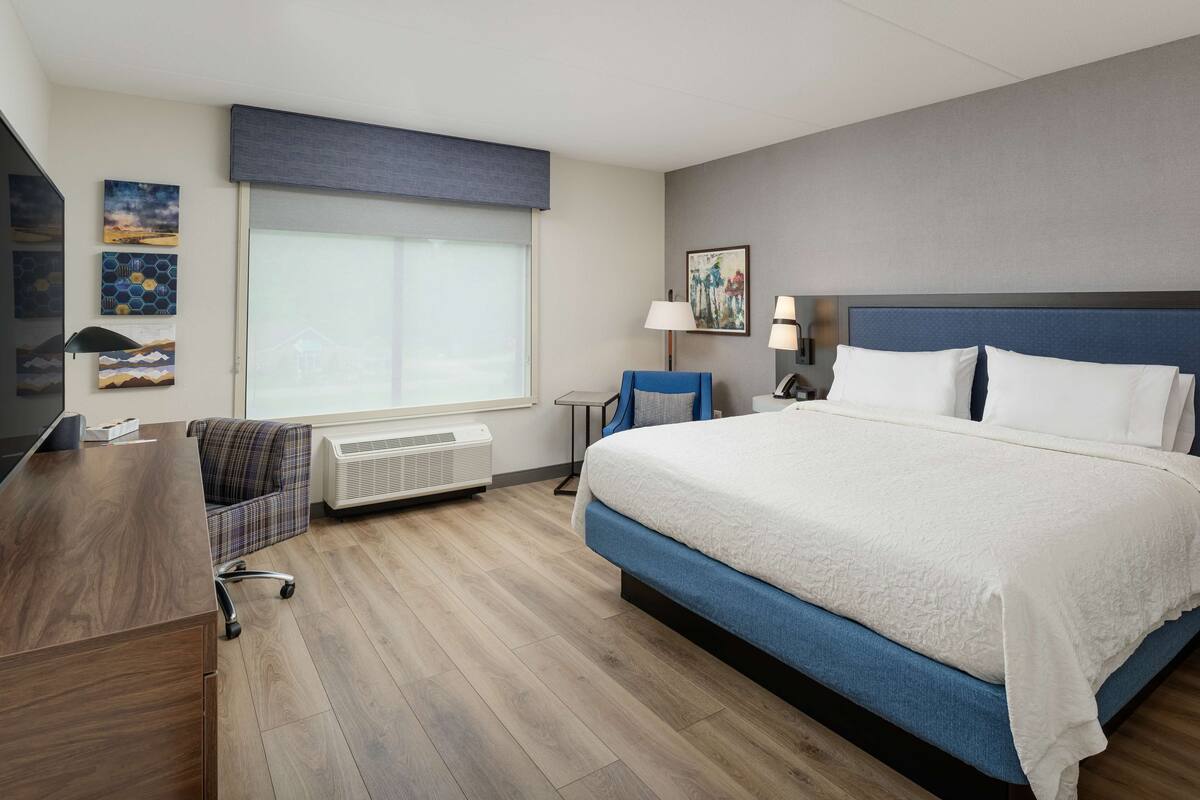 Quarto de hotel com uma cama grande, uma escrivaninha e uma cadeira. Há uma janela com vista para o exterior.