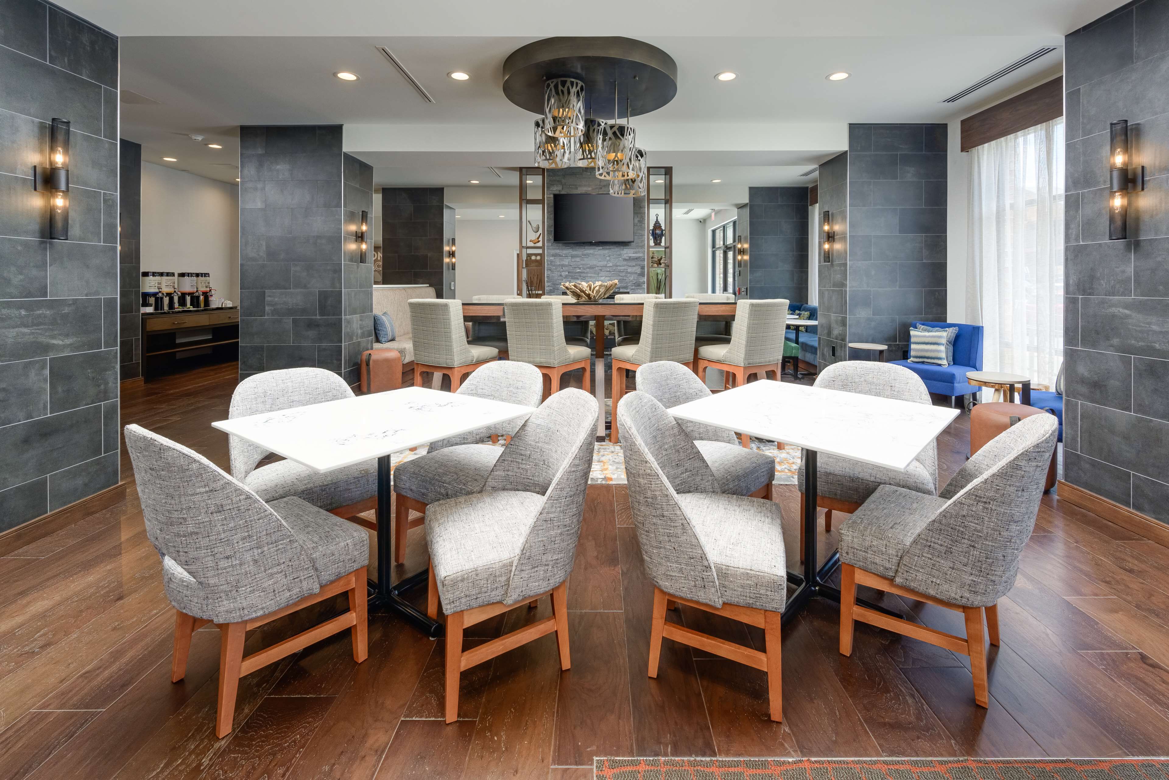 Uma sala de jantar moderna com uma mesa central e seis cadeiras cinzas estofadas.