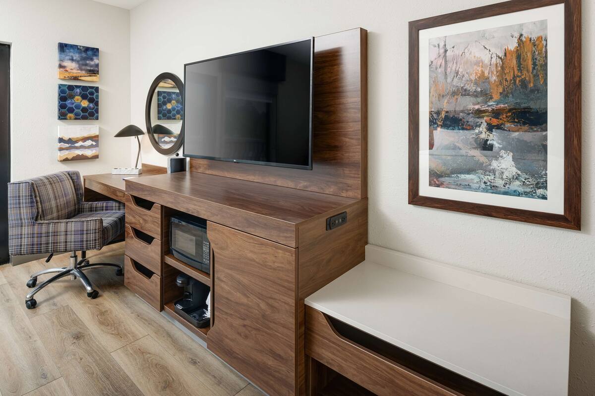 Uma sala de estar moderna com uma grande TV de tela plana montada em um armário de madeira, uma poltrona xadrez e um quadro abstrato emoldurado na parede.