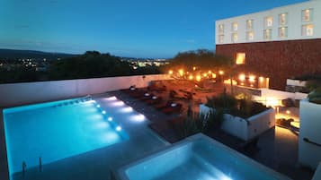Área de piscina no terraço com espreguiçadeiras e vista da cidade ao entardecer.
