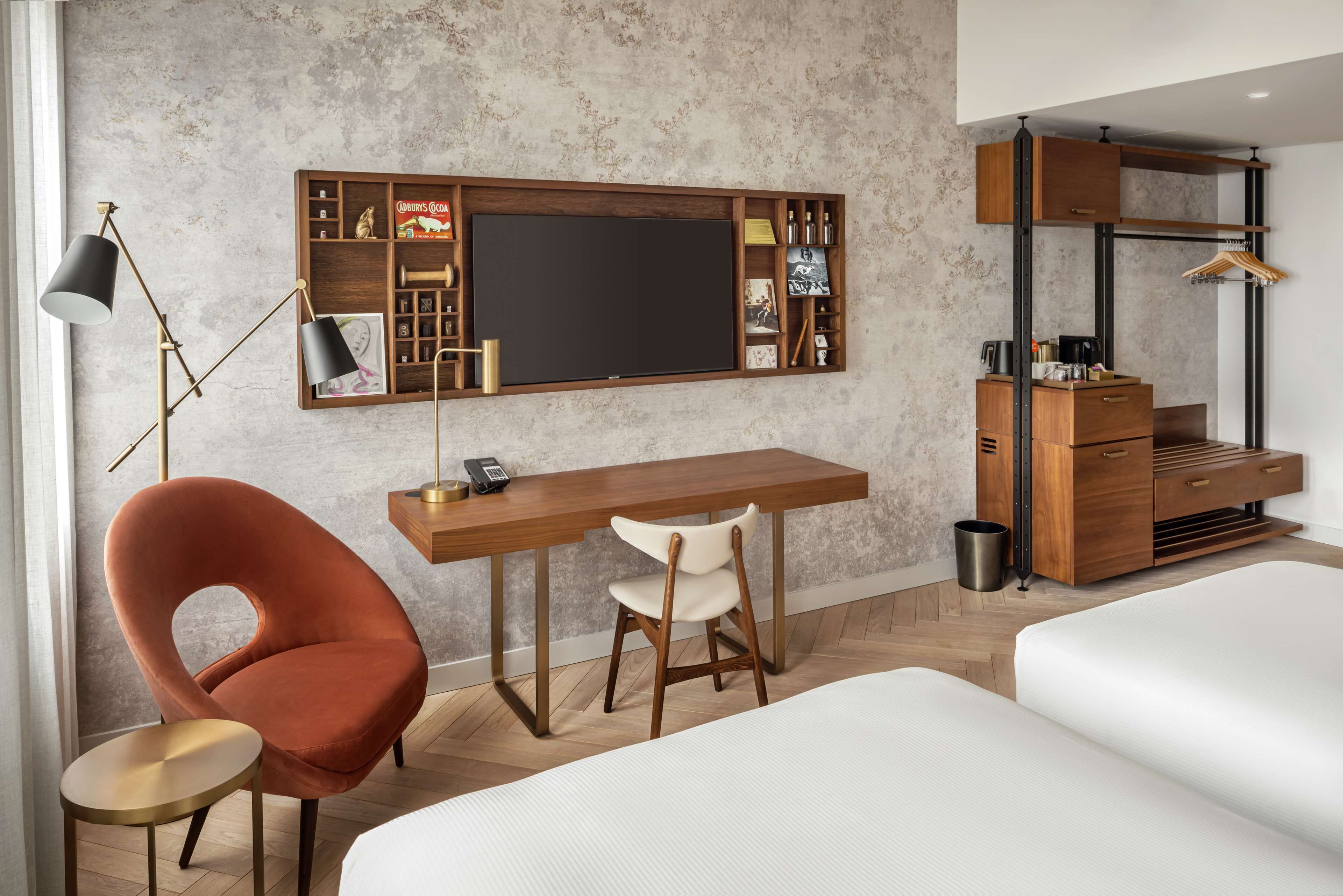 Quarto de hotel moderno com escrivaninha de madeira, uma cadeira vermelha, cama e guarda-roupa com espaço para pendurar.