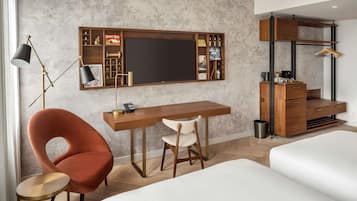 Quarto de hotel moderno com escrivaninha de madeira, uma cadeira vermelha, cama e guarda-roupa com espaço para pendurar.