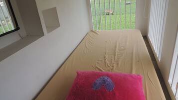 Quarto pequeno com uma cama de solteiro e janela com vista para uma área gramada.
