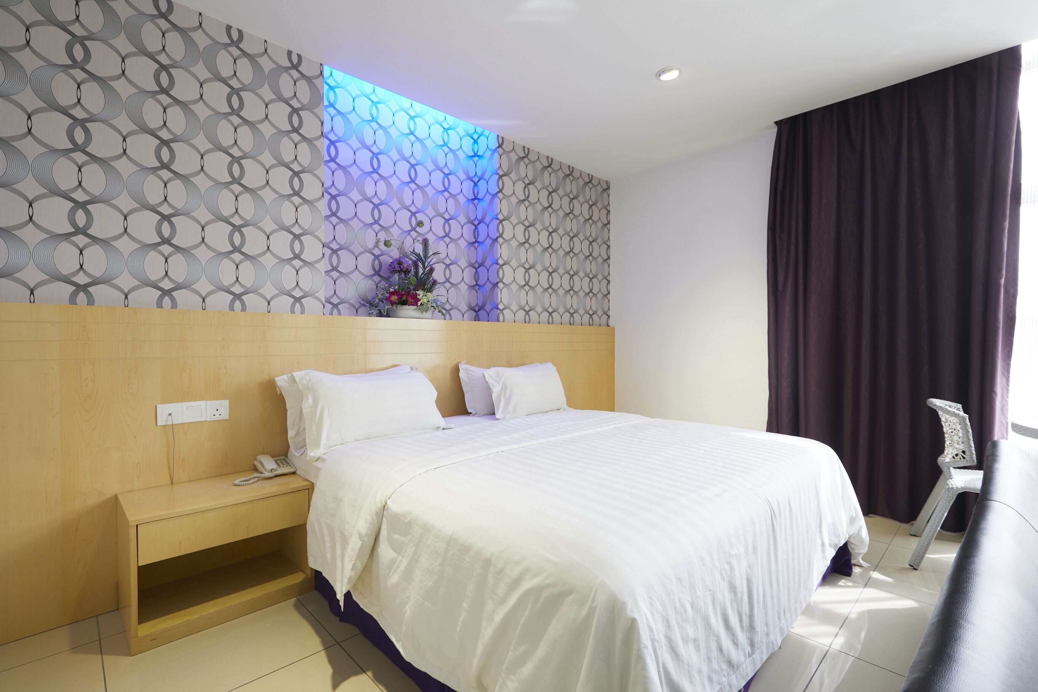 Quarto de hotel com cama grande, mesa de cabeceira de madeira, telefone e parede decorativa com padrão geométrico.