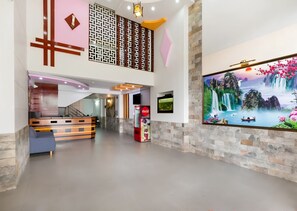 Um hall de hotel com balcão de recepção, área de estar e um grande mural de uma cascata.