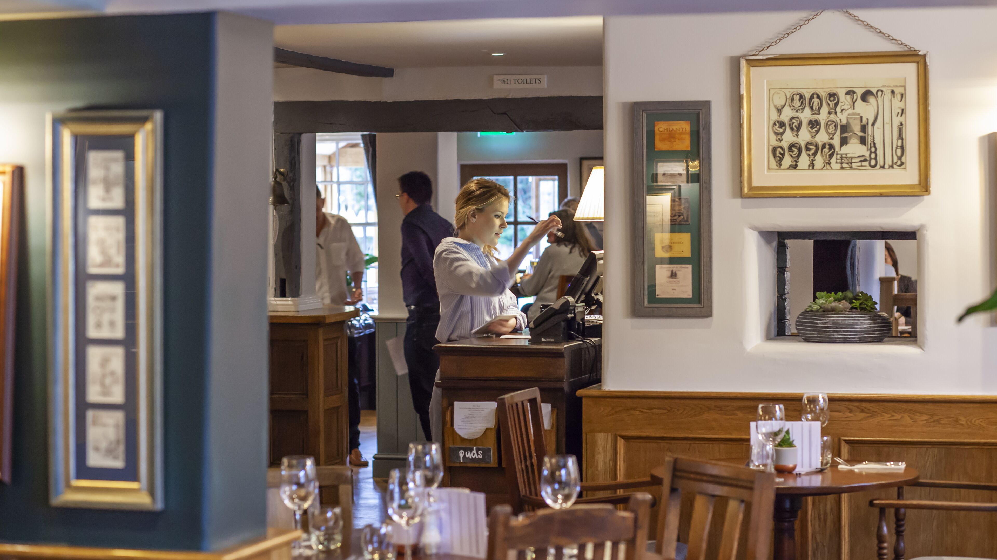 Interior de restaurante com mobiliário de madeira, obras de arte emolduradas nas paredes e um quadro de menu.