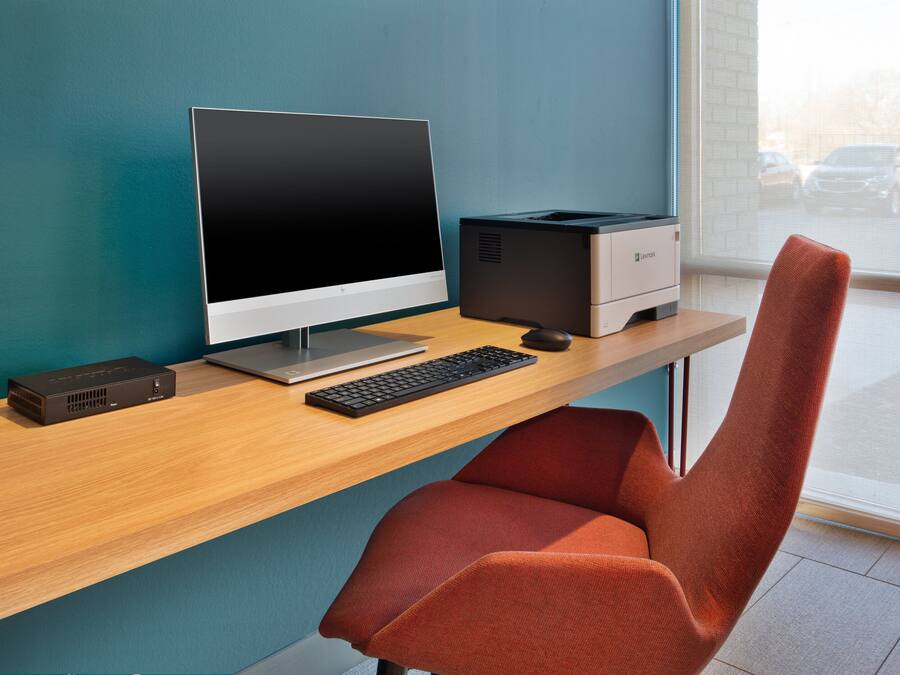 Uma mesa de escritório moderna com um computador, uma impressora e uma cadeira de escritório vermelha.