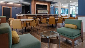 Um saguão de hotel moderno com área de bar, sofás e uma grande janela que ilumina naturalmente o espaço.