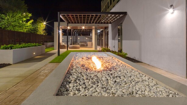 Uma área de estar moderna ao ar livre, com lareira, assentos e pérgola.