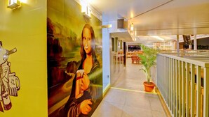Um corredor com um mural da Mona Lisa, um aviso de banheiro e uma planta em vaso.