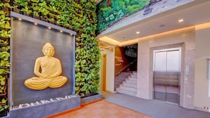 Um lobby moderno com uma grande estátua de Buda, uma escadaria e uma parede com plantas.