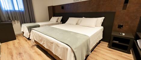 Quarto de hotel com duas camas, piso de madeira, cabeceira escura e uma frase decorativa na parede.