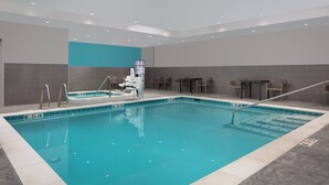 Piscina interior com água azul cristalina, prancha de mergulho e área de estar com cadeiras e mesas.